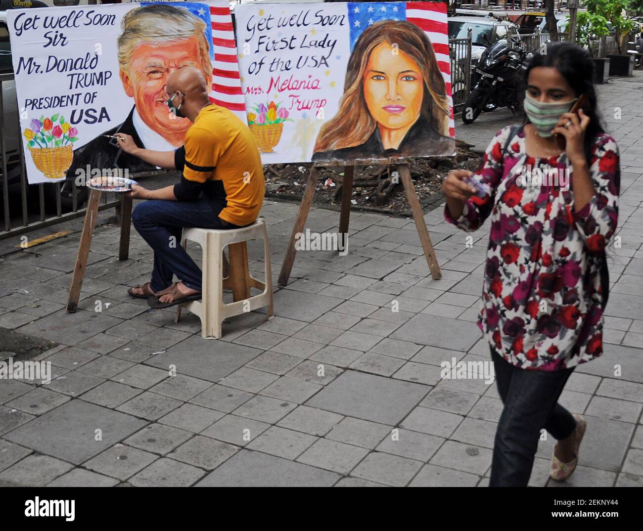 A woman walk past an artist painting posters of the US President Donald ...