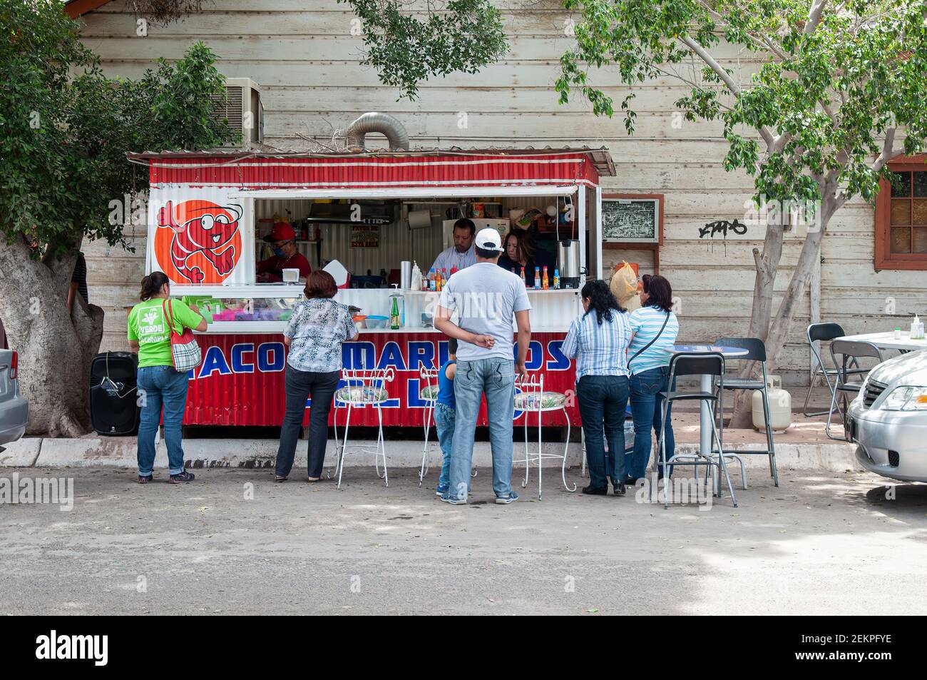 People wait by a red and white taco stand for their food in Mexico ...