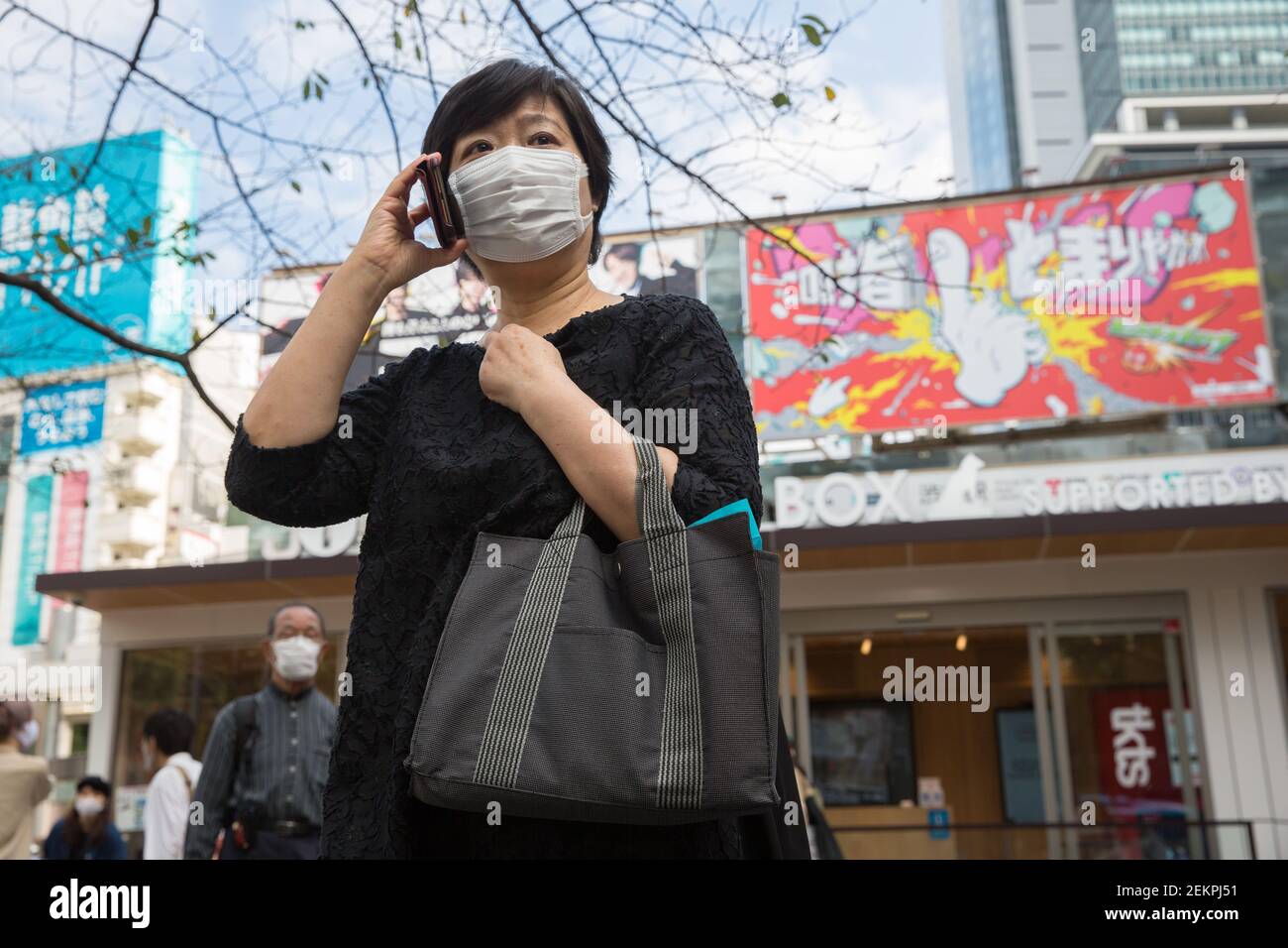A woman wearing a face mask while talking on stands in front of a newly ...