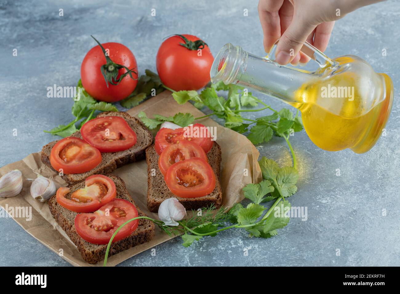 Hand pouring a bottle of oil in toast with tomatoes Stock Photo - Alamy