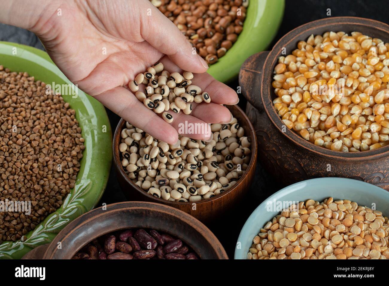 Different kinds of bean seeds, lentil, peas in dishes on a dark ...