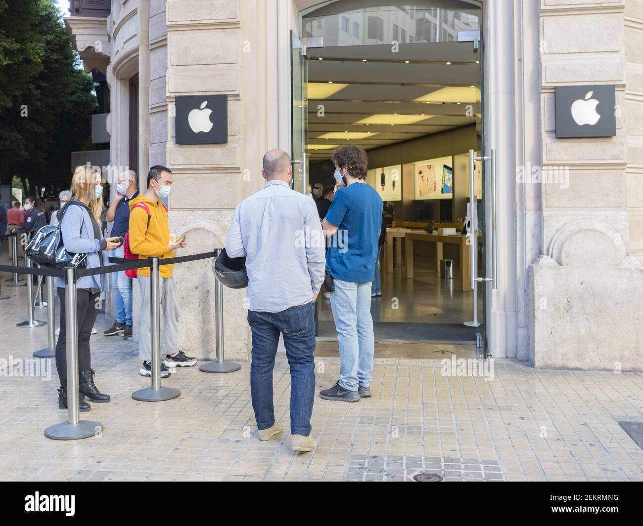 People wearing face masks queue outside the Apple store on Colon Street ...