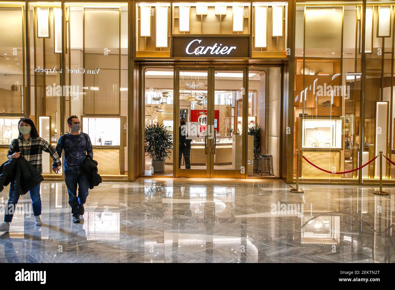 Shoppers wearing face masks walk past the Cartier logo and store seen ...