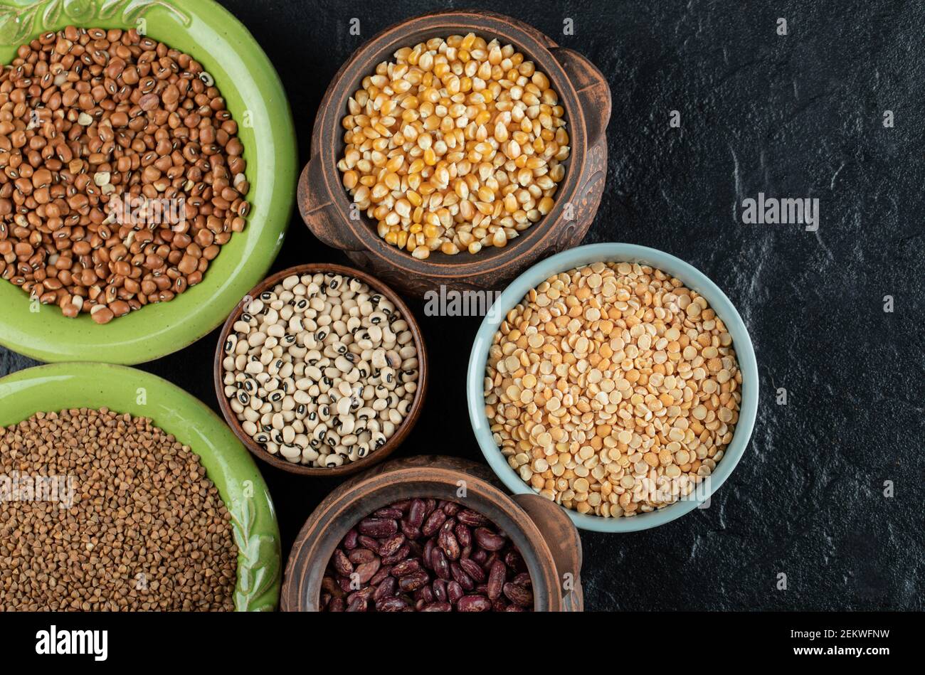 Different kinds of bean seeds, lentil, peas in dishes on a dark ...