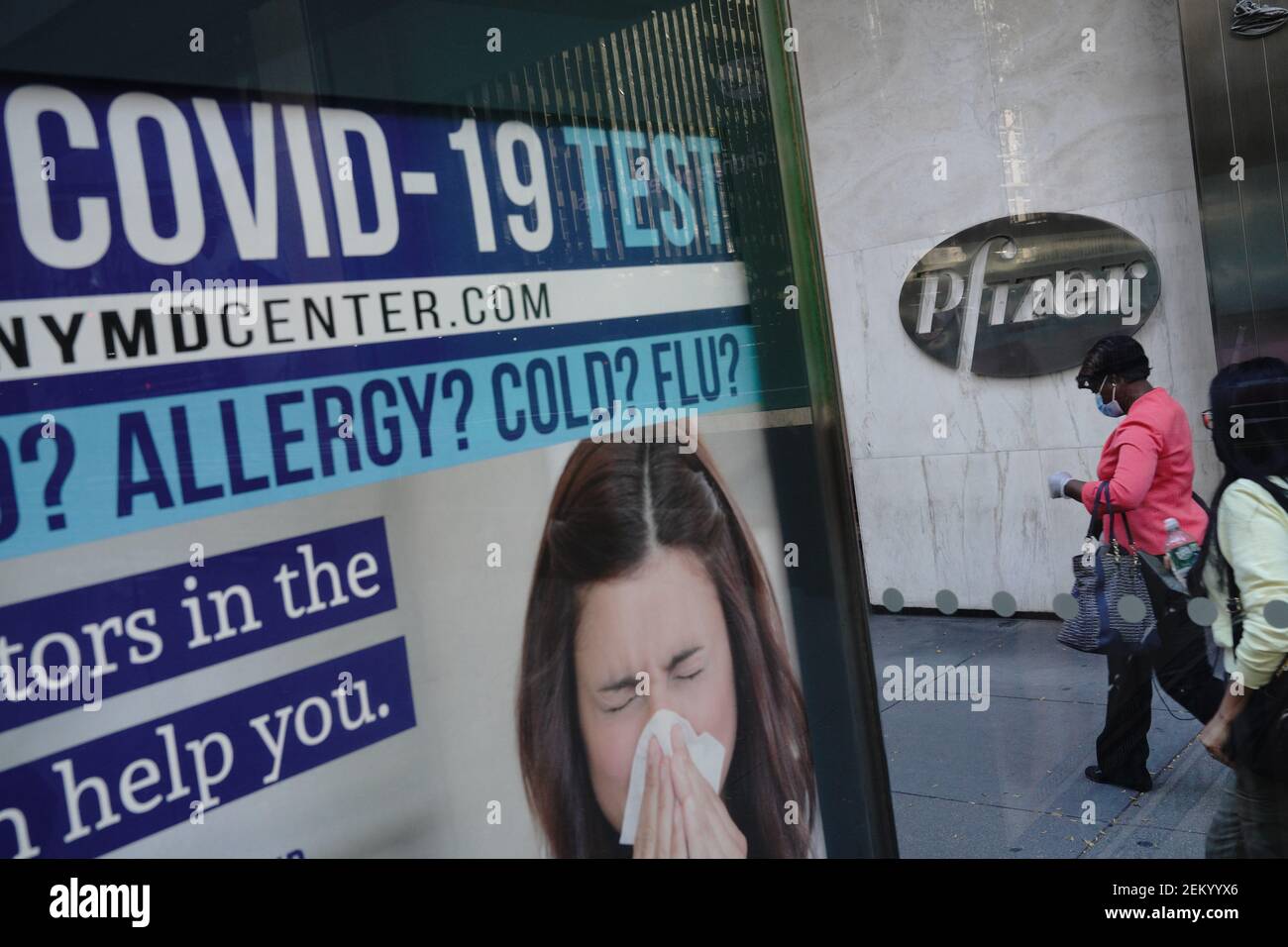 People wearing masks walks past a Pfizer sign outside their ...