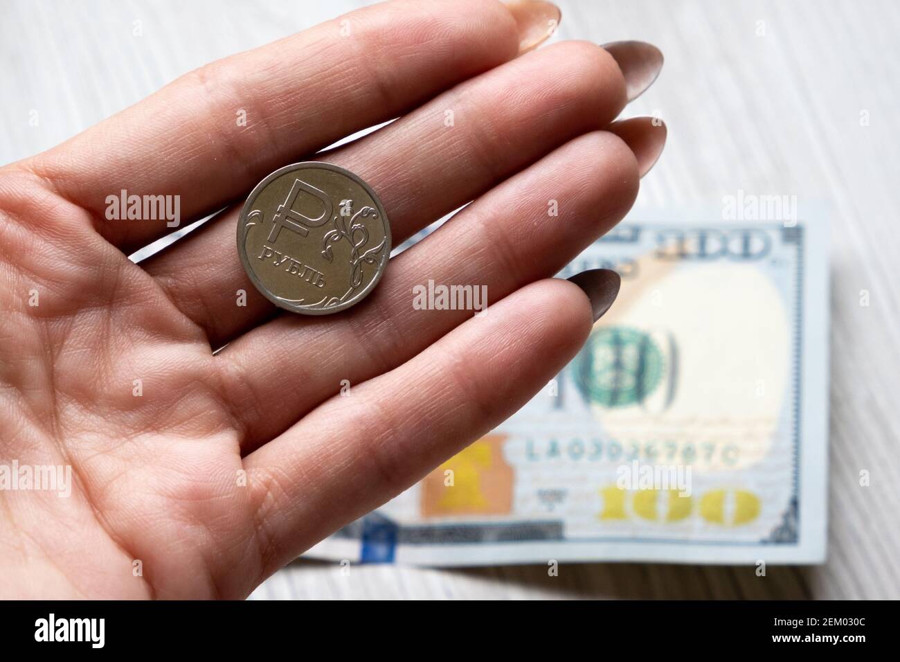 a female hand holds a Russian one ruble coin over a hundred dollar bill ...