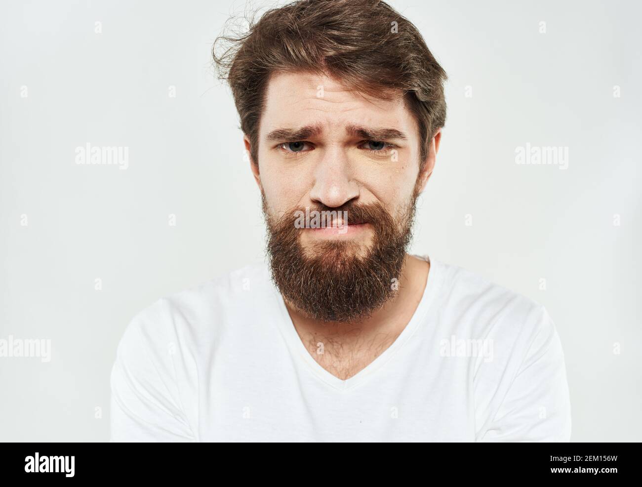 Bearded man in a white T-shirt on a light background sad face emotions ...