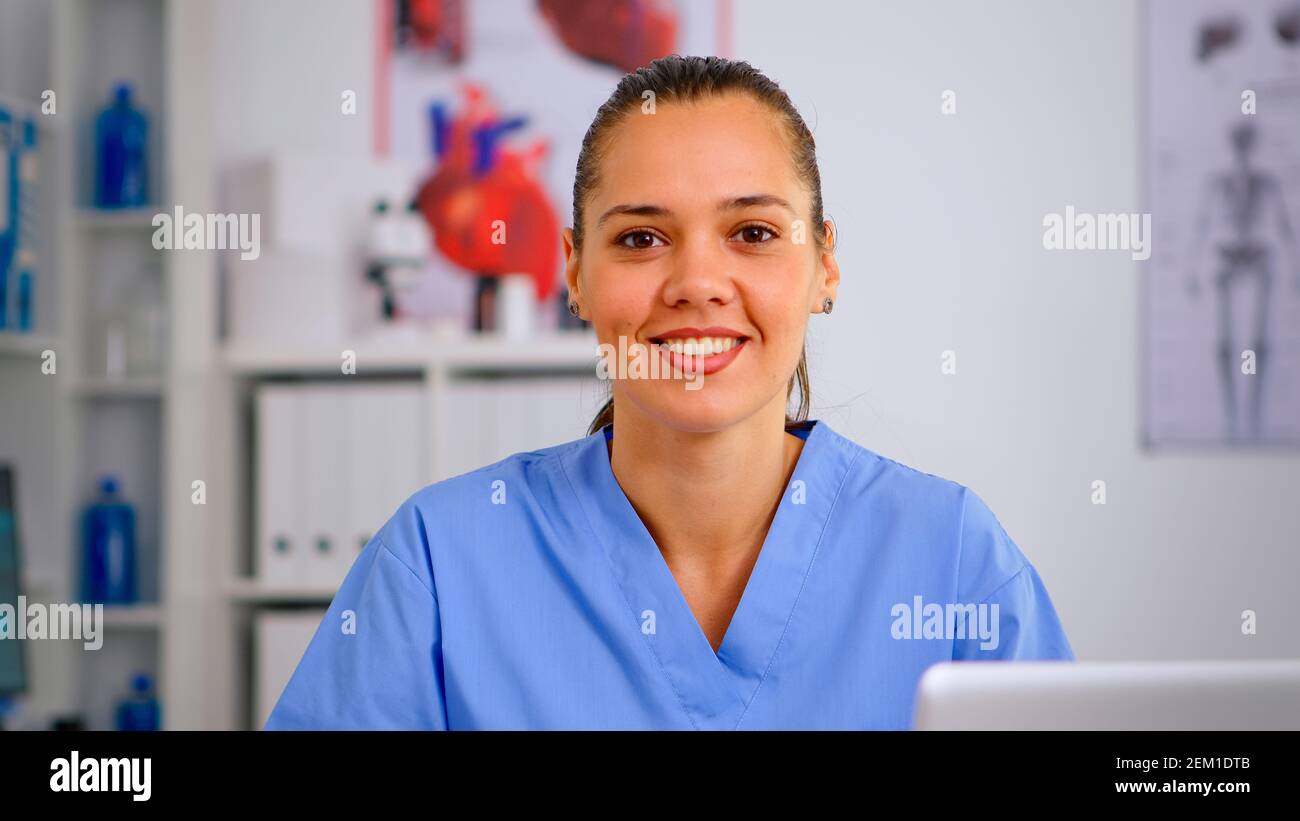 Portrait of nurse looking at camera smiling after typing on laptop ...