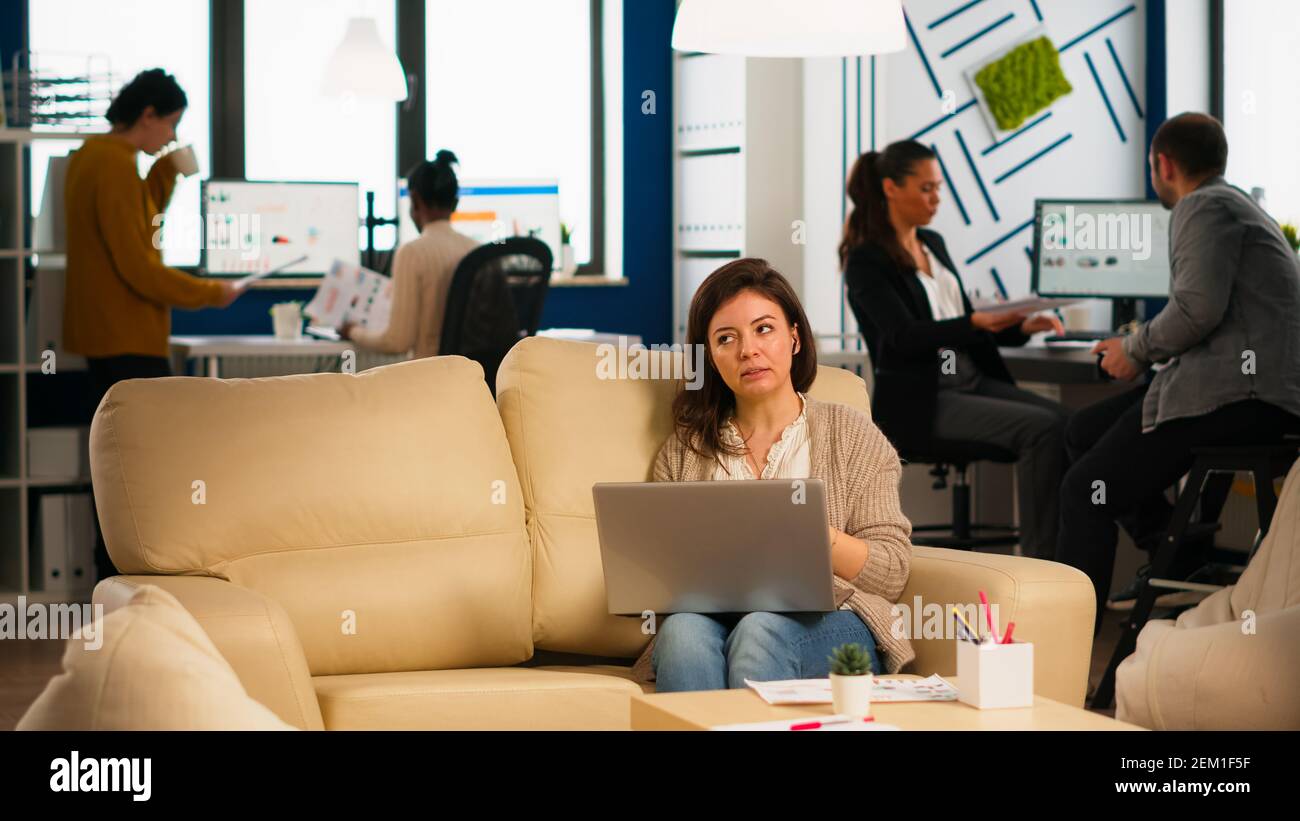 Manager woman sitting on couch holding laptop and talking on video call ...