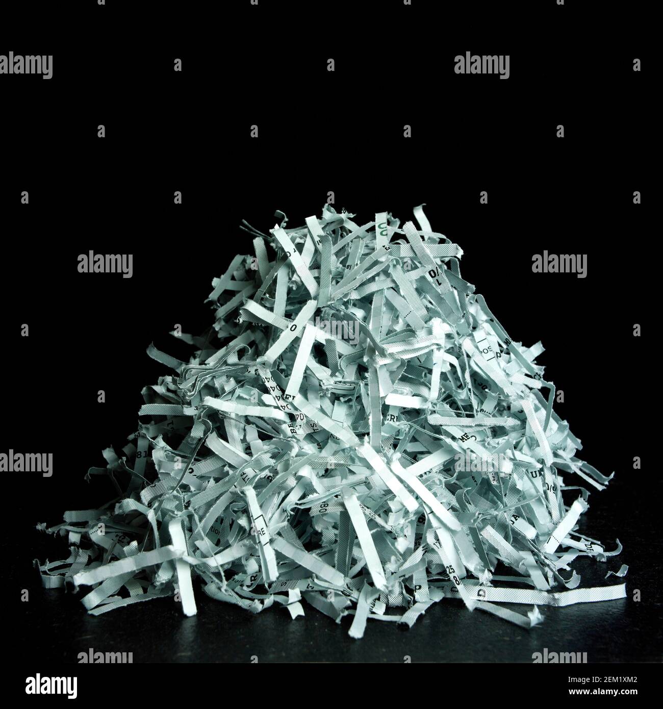 A large mound of shredded paper sits on a black surface in a dimly lit ...