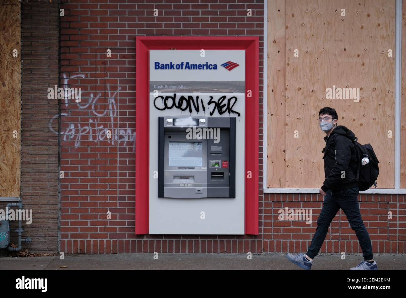 A man walks past Bank of America ATM with "colonizer" graffiti on ...