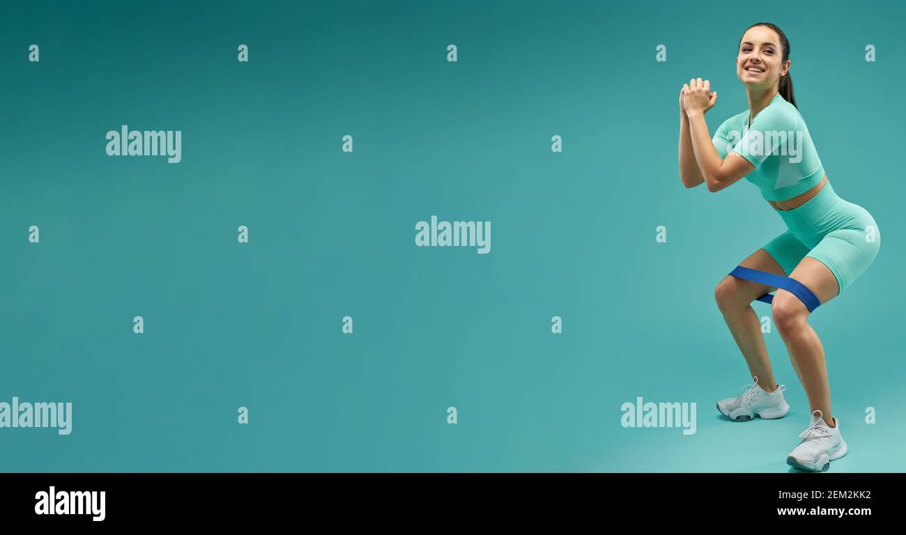 Beautiful sporty lady using elastic fitness band while doing squats and ...