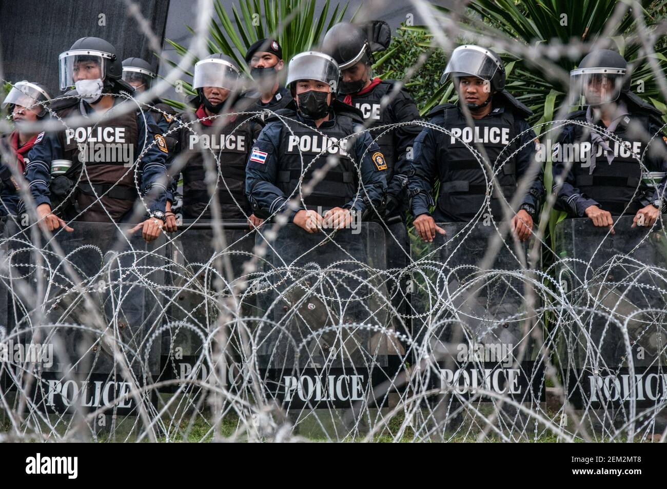 Riot policemen stand on guard behind the barbed wire fence in front of ...