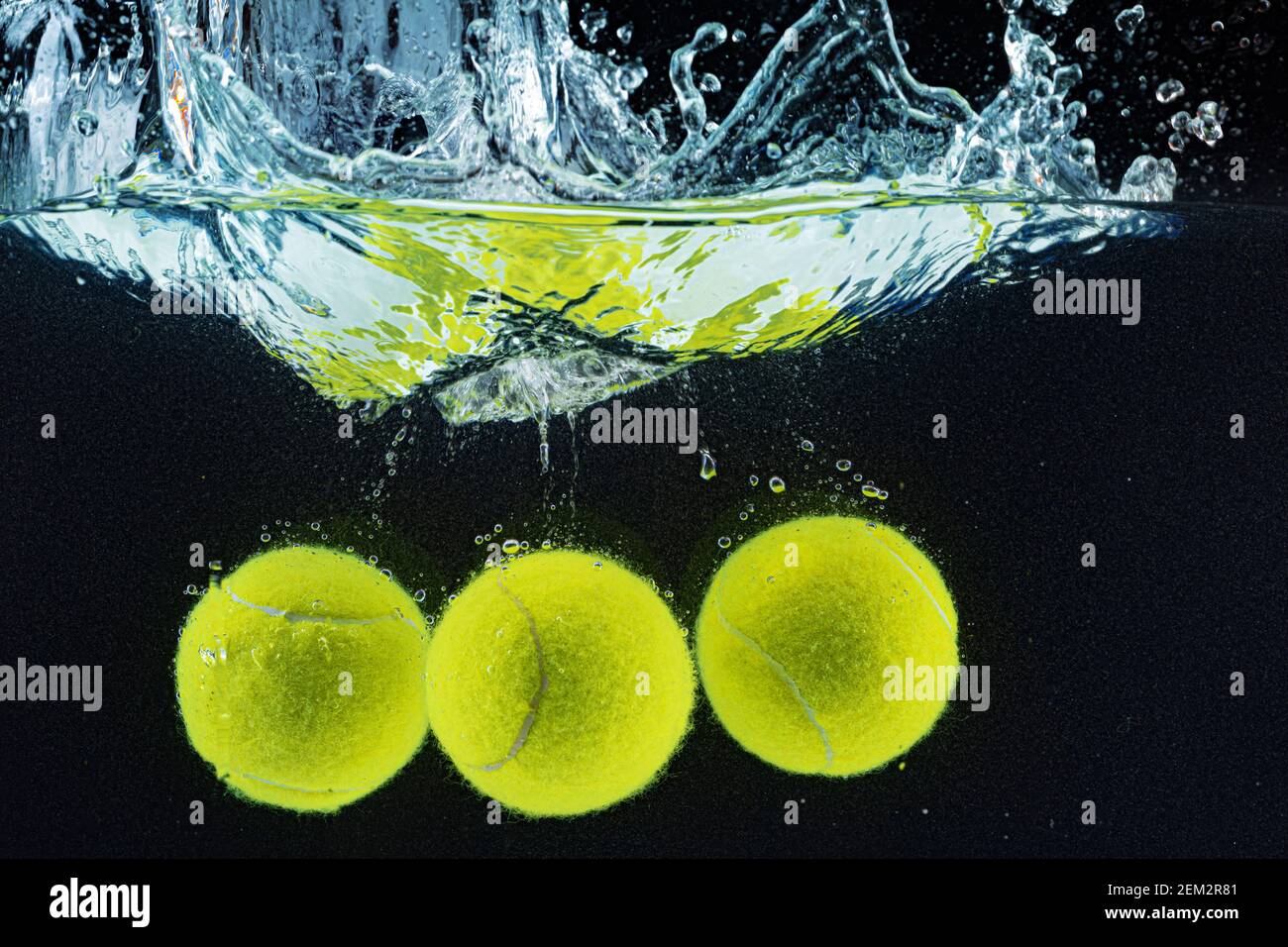 Tennis ball falling in water with a splash against dark background ...
