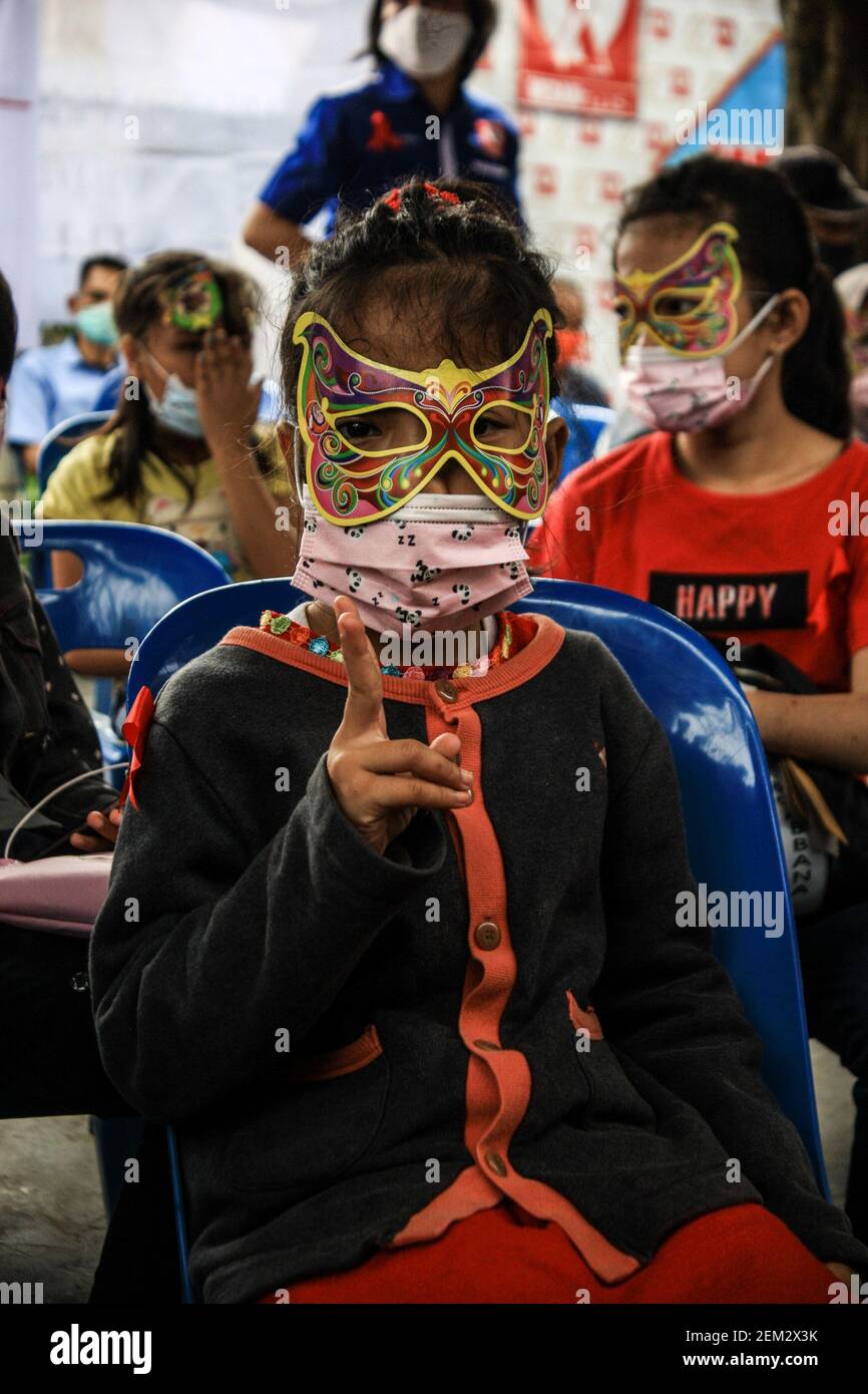 A young girl wearing a mask shows a peace sign with her fingers during ...