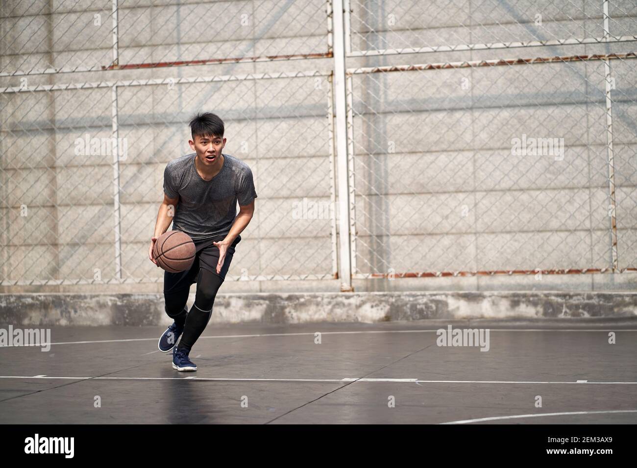 young asian man basketball player attempting a dunk on outdoor court ...