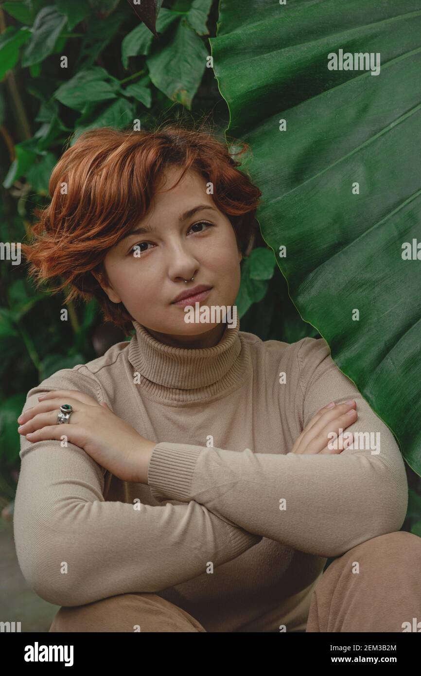 A beautiful plus size girl with red hair among green branches of ...