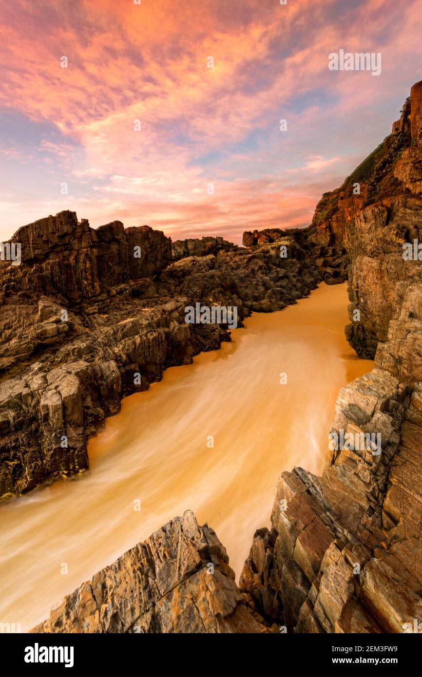 Water rushes up a steeply sloping rocky embankment on the beach Stock ...