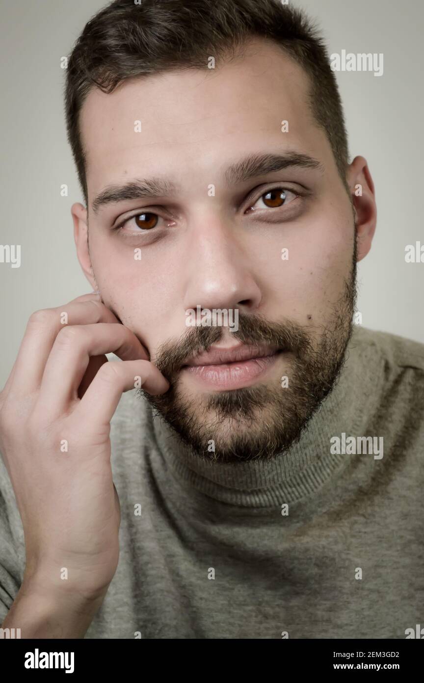 Portrait of a young man with a short beard with his hand on his cheek ...