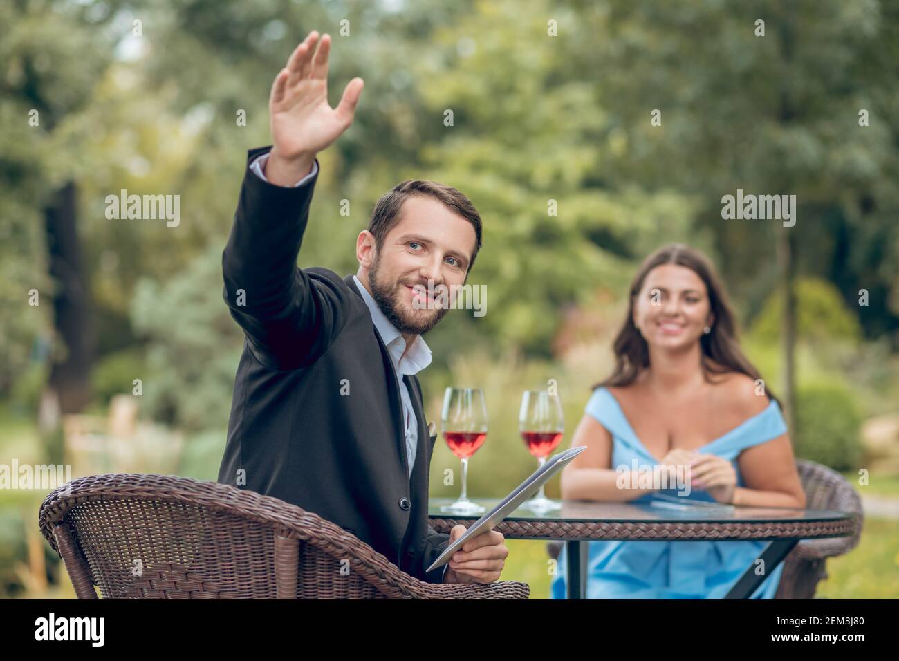 Smiling man with menu raising hand and woman Stock Photo - Alamy