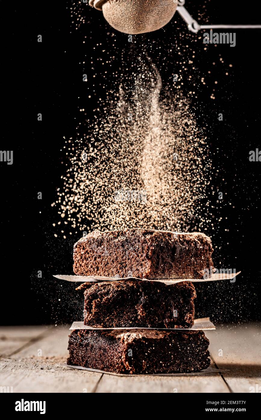 Chocolate powder spread on top of brownies on wooden table and black ...