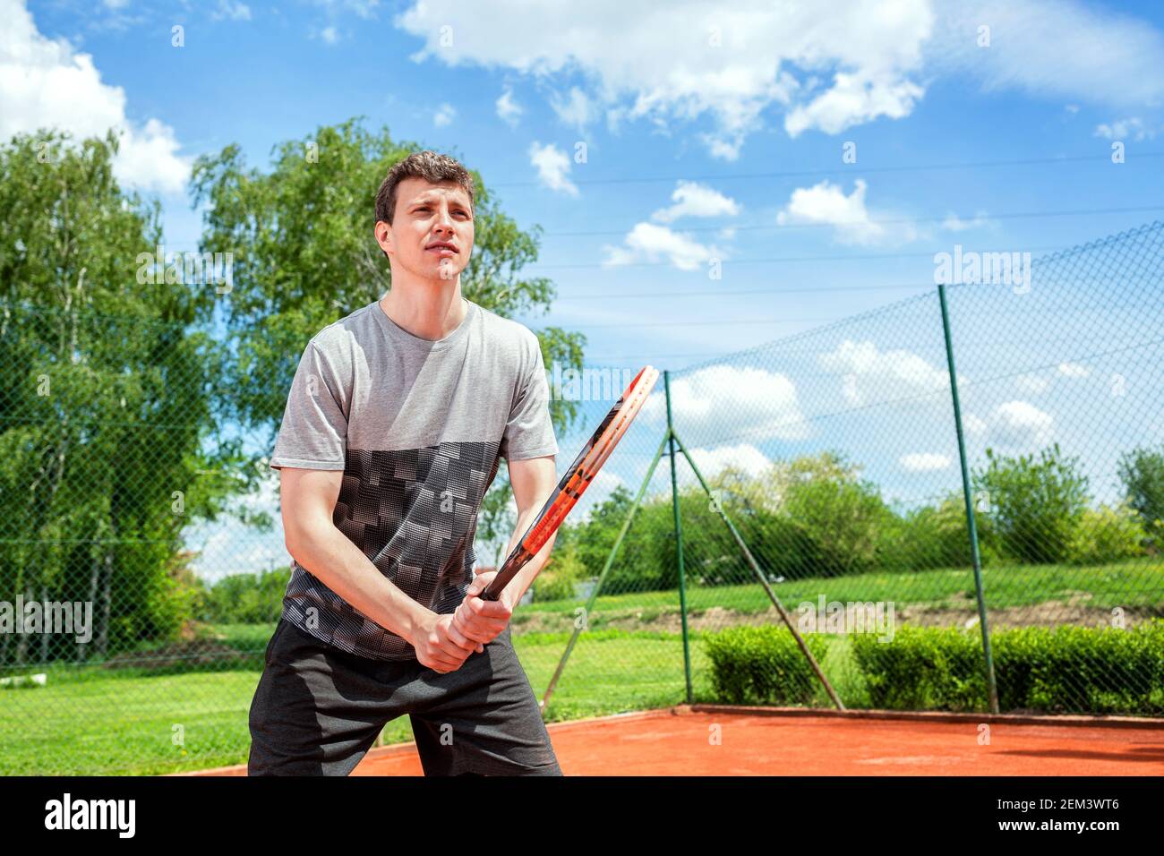 Young guy dressed in gray-black outfit holding a tennis racket while ...