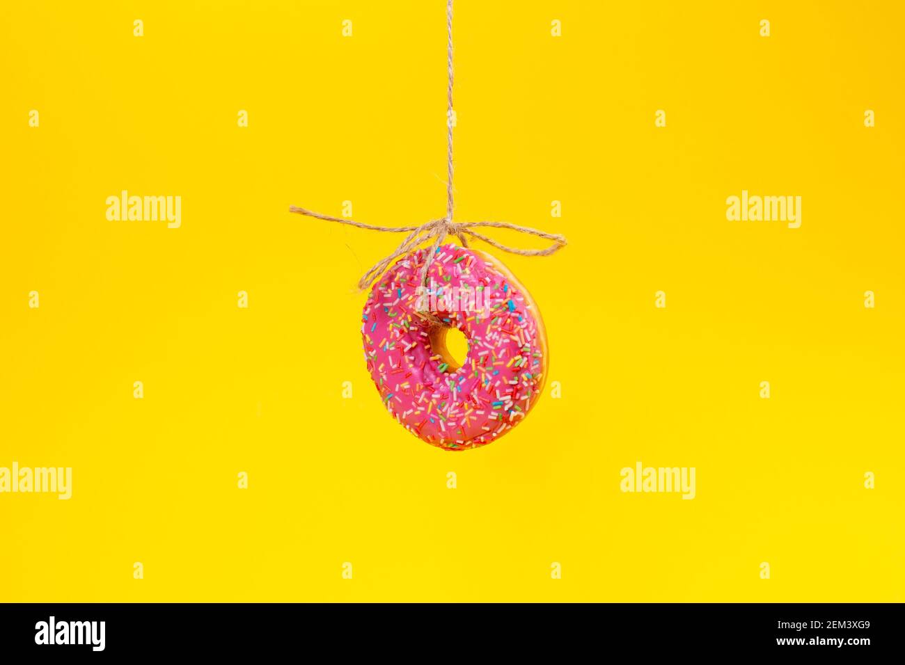 Sweets and candys. A round doughnut with pink frosting, suspended on a ...