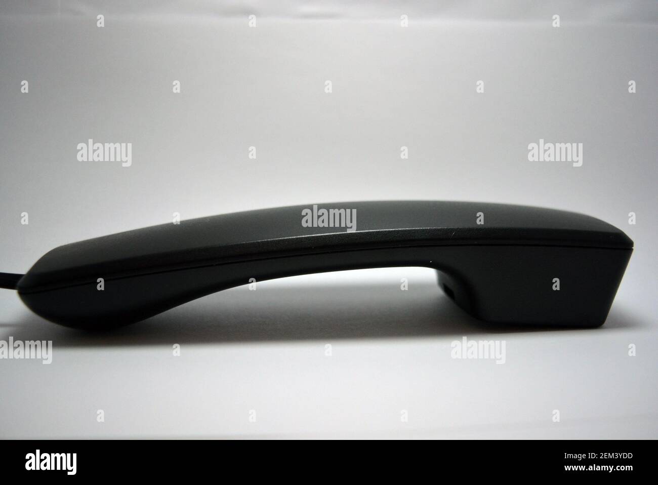 A black telephone receiver from a landline telephone lies on a white ...