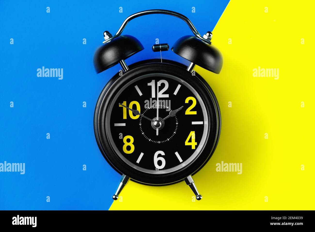 Black round metal alarm clock on legs on a bright composite background ...