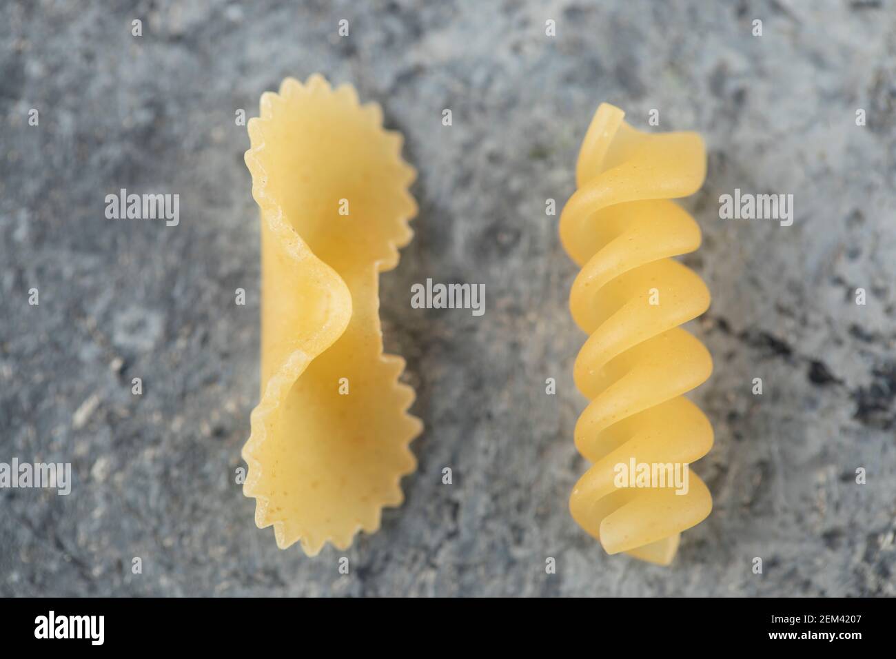 Raw dry fusilli spirale pasta and farfalle tonde on a marble background ...