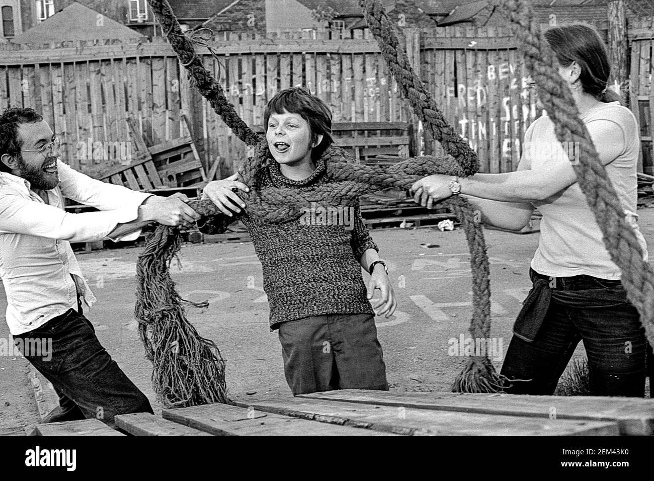 Childrens Adventure Playground supervisors having fun with boy pretence ...