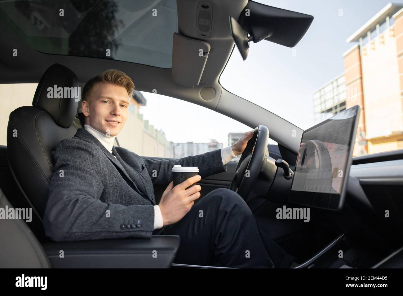 Handsome Caucasian man sitting in modern self-steering electric vehicle ...