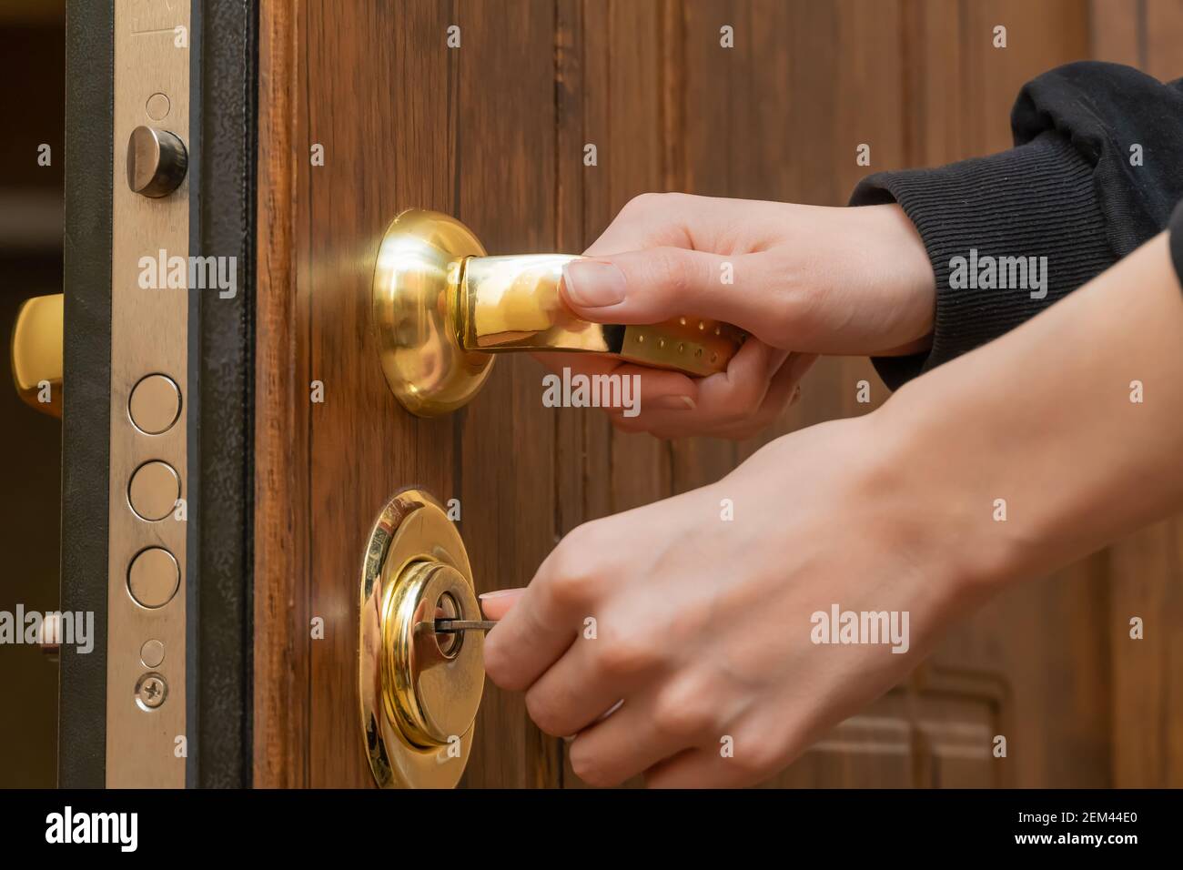 Woman's hands open a brown front door with a gold handle with a key ...