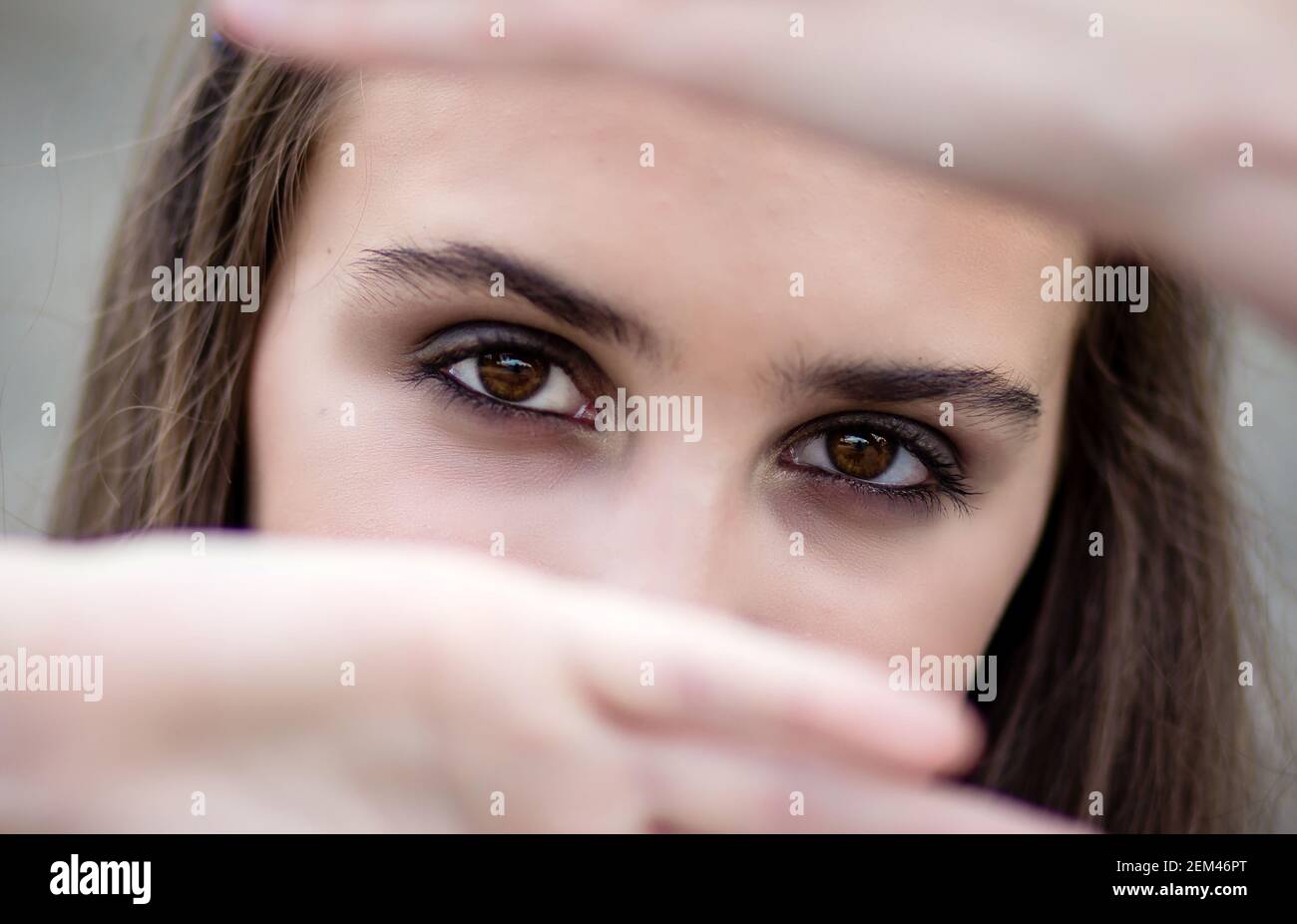 Close-up of brunette girl. Focus on her eyes. Look through her hands ...