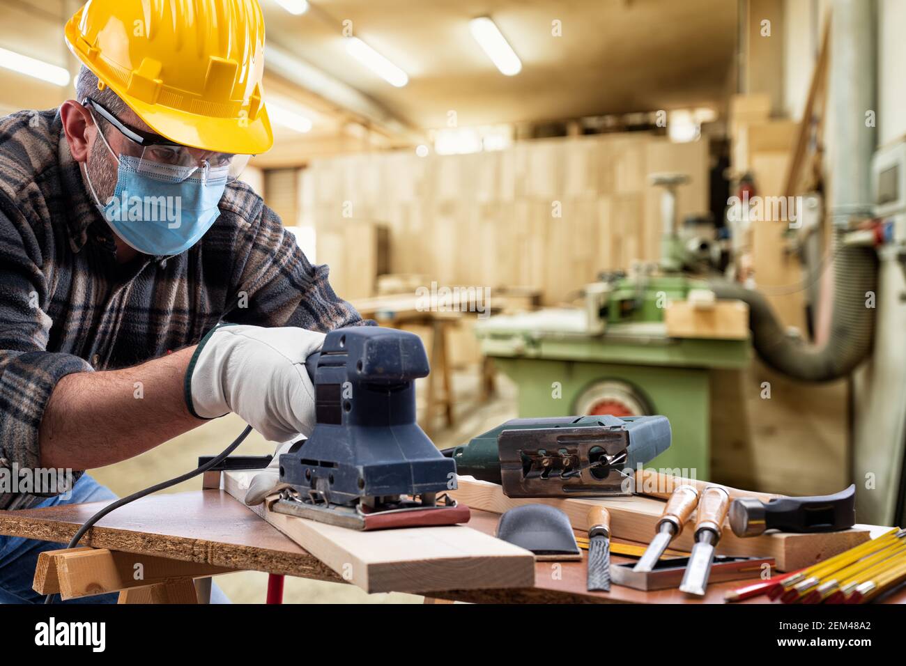 Carpenter worker at work in the carpentry workshop, wears helmet ...