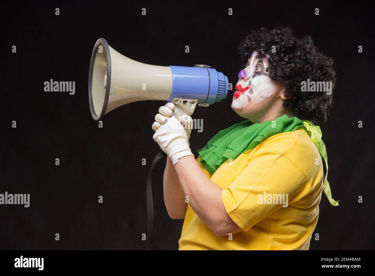 Scary evil clown shouting into a megaphone on a black background Stock ...