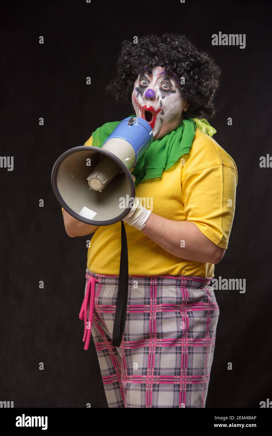 Scary evil clown shouting into a megaphone on a black background Stock ...