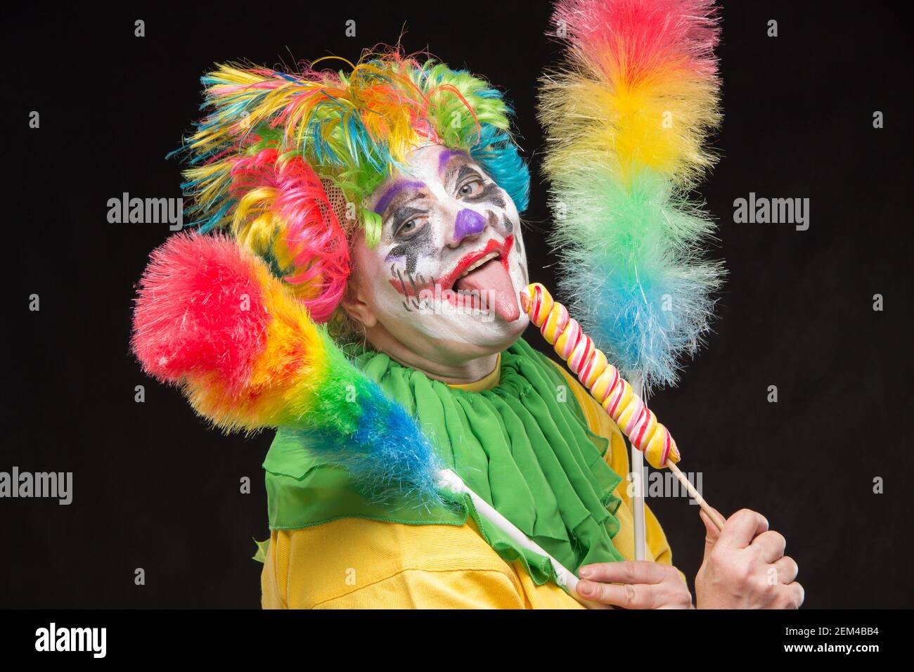 Scary clown with colorful mohawk and a smile with a lollipop on a black ...