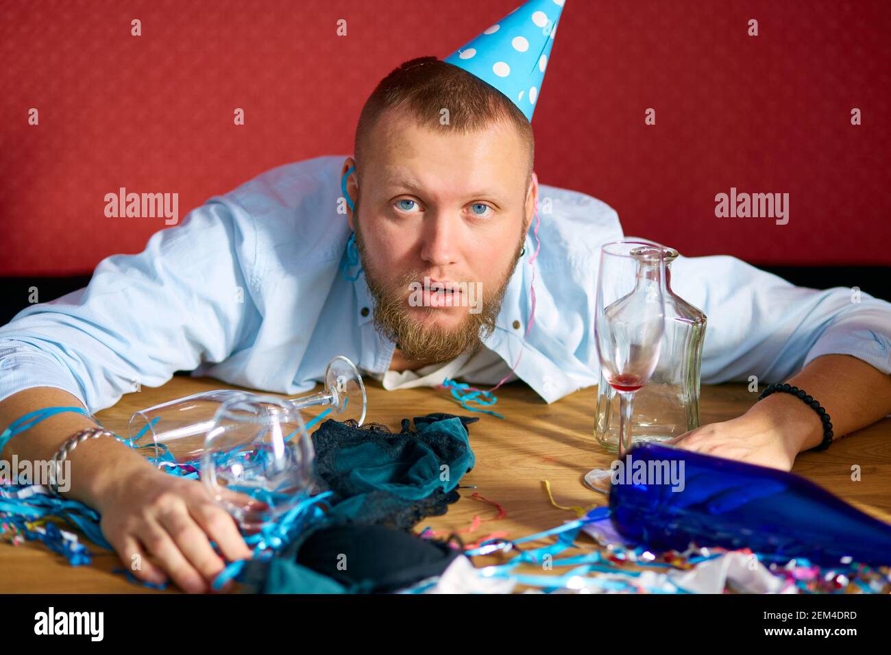 Tired man at table with blue cap in messy room after birthday party ...