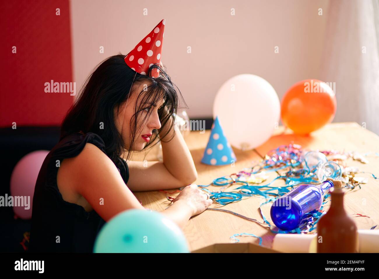 Young woman with red rubbed lipstick and cap, sitting tired at table in ...