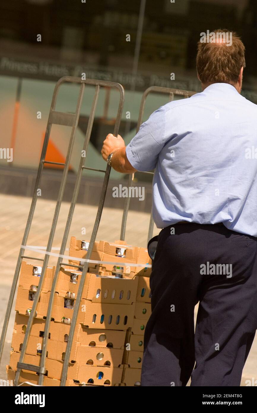 Rear view of a man pushing a stack of crates in a push cart Stock Photo ...
