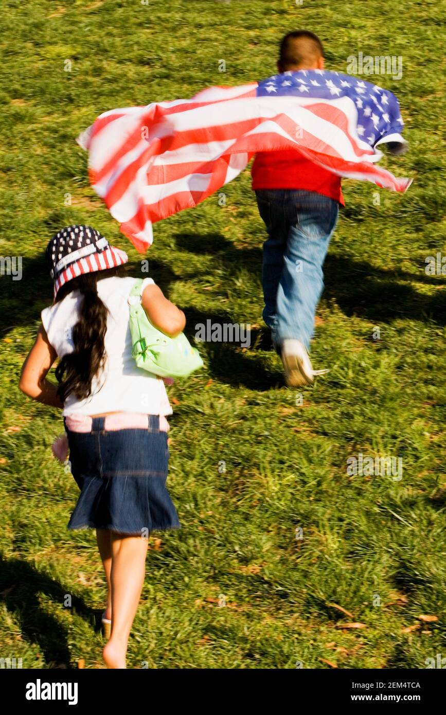 Rear view of a boy running with an American flag and a girl behind him ...