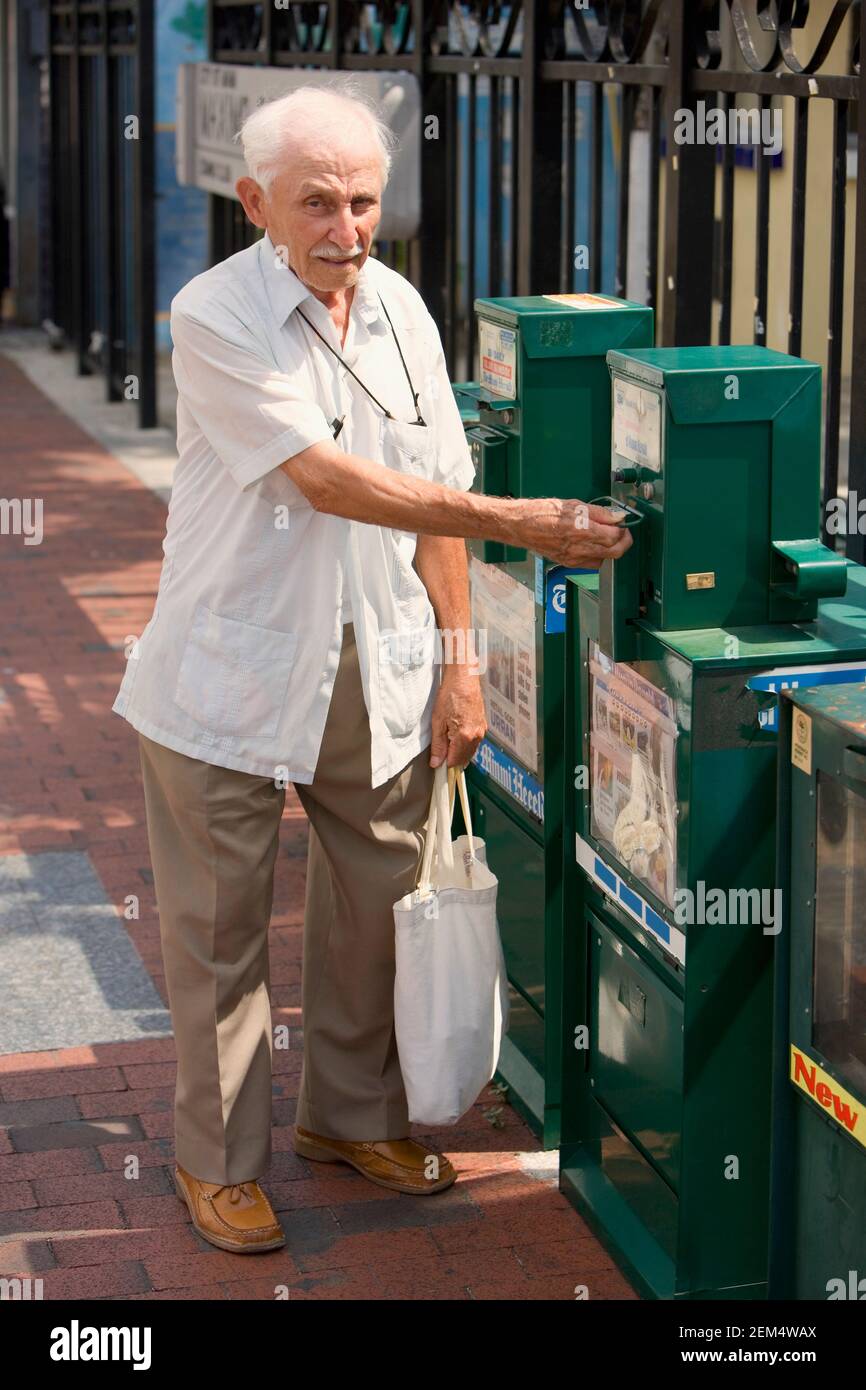 Portrait of a senior man standing beside newspaper vending machines ...