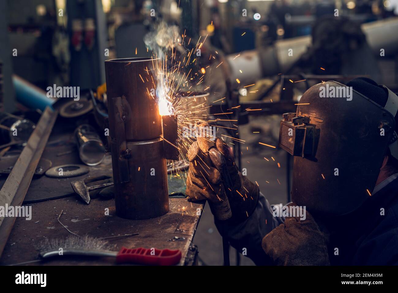 Welder in protective uniform and mask welding metal pipe on the ...