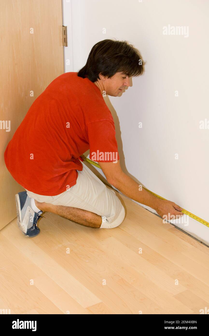 Side profile of a mid adult man measuring a wall with a tape measure ...