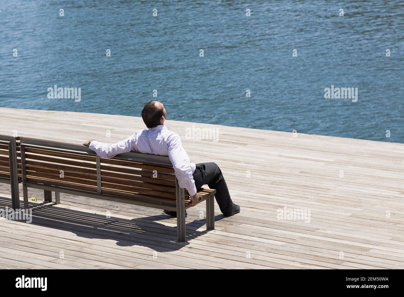Rear view of a man sitting on a bench at the riverside, Barcelona ...