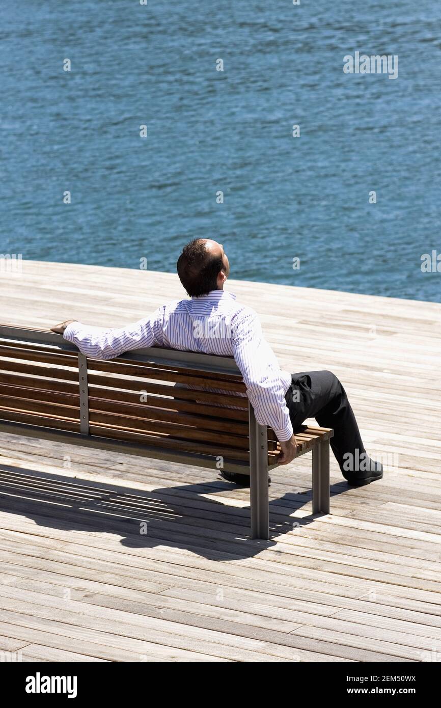 Rear view of a man sitting on a bench at the riverside, Barcelona ...