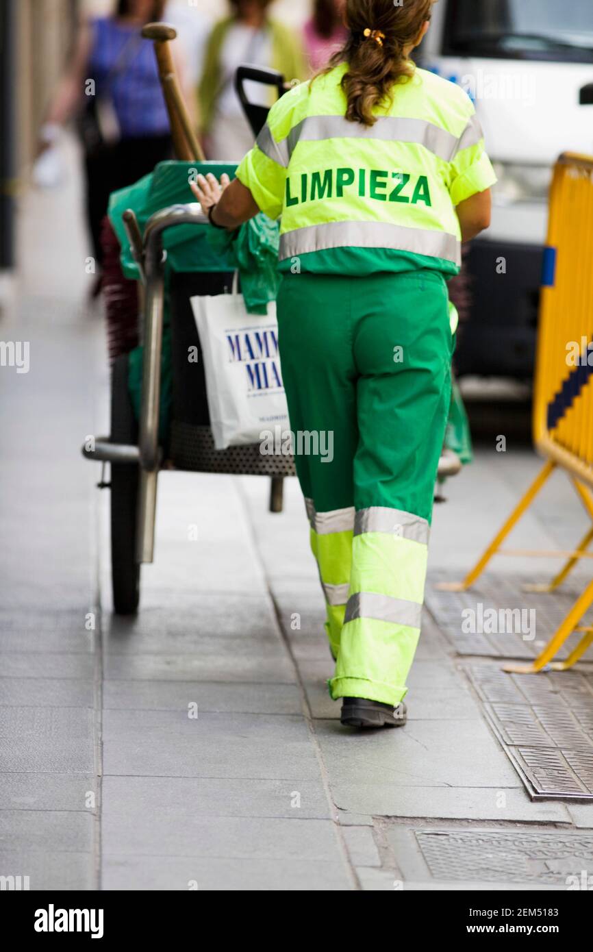 Rear view of a female street sweeper pushing a garbage can, Madrid ...