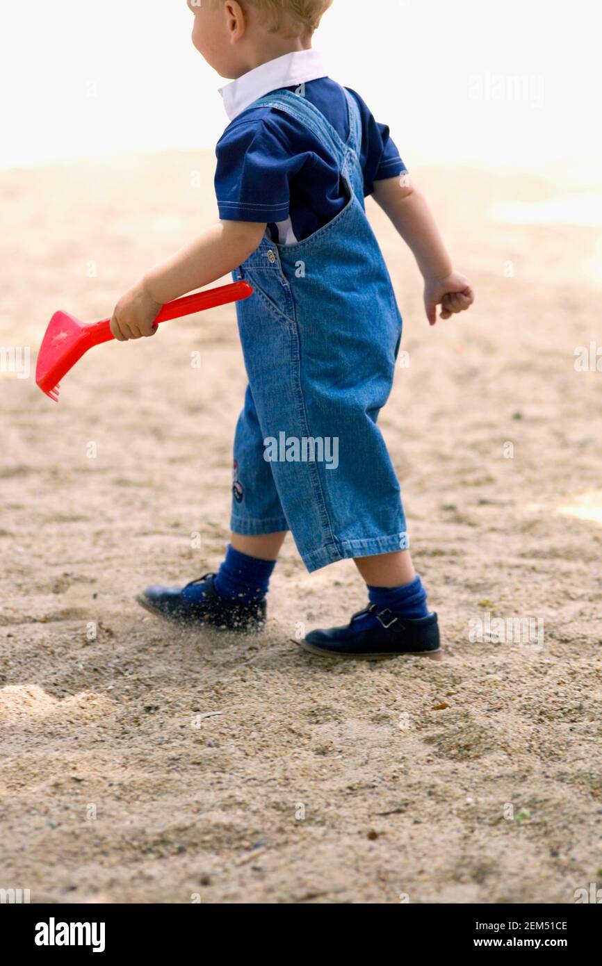 Side profile of a boy holding a plastic shovel and walking on sand ...