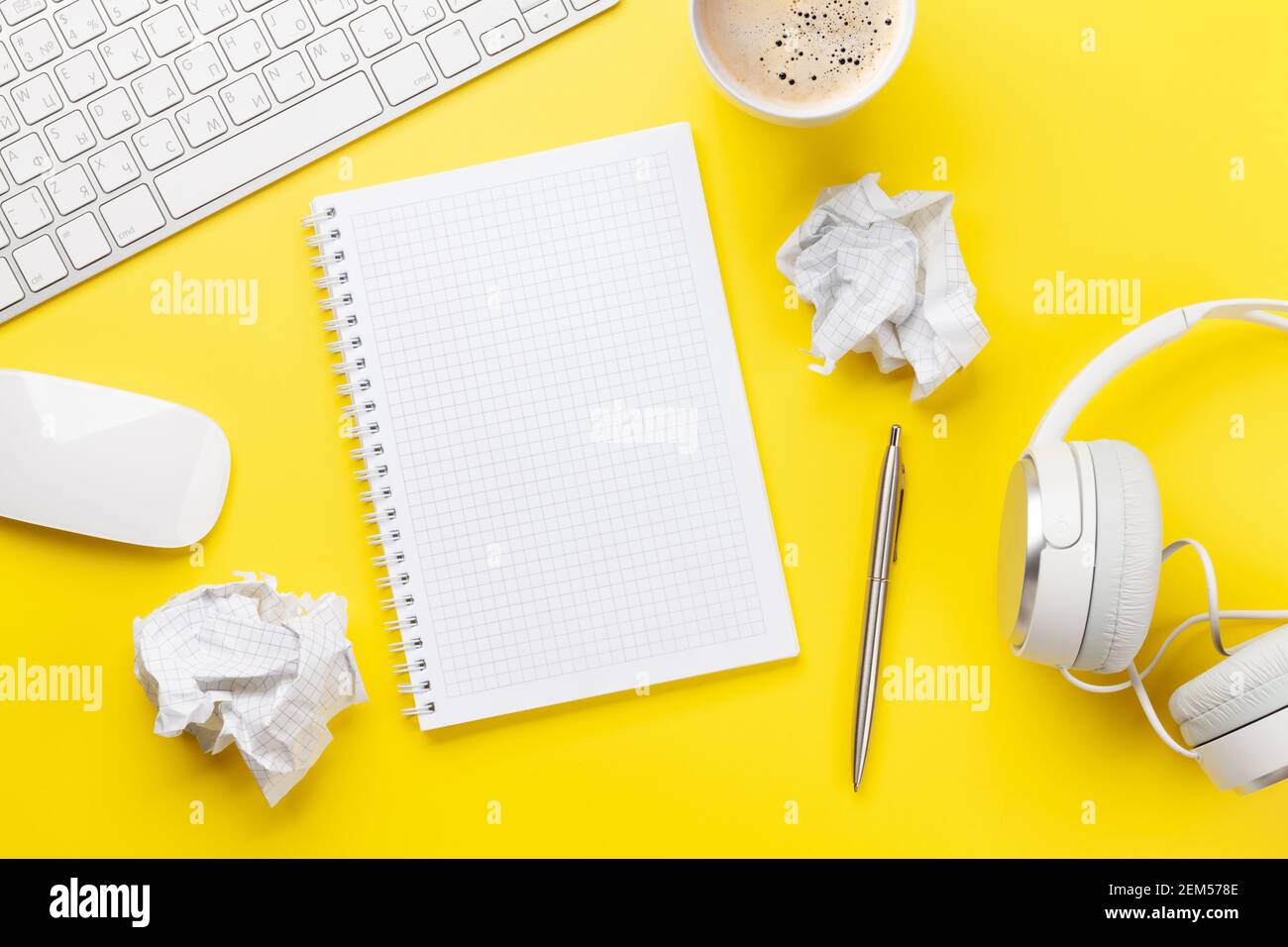Office desk with supplies, headphones and blank notepad over yellow ...
